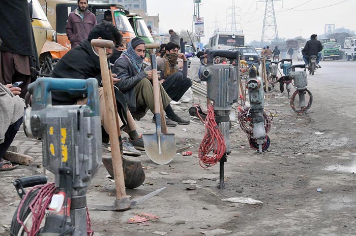Labourers alongwith their tools sitting on roadside waiting for clients ...