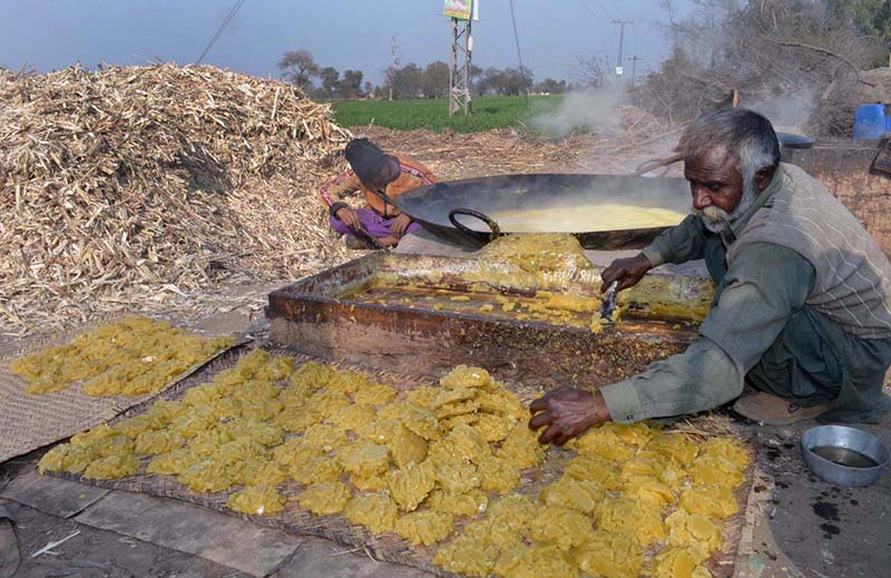 Farmers busy making traditional sweet item (Gurr) on his roadside setup ...