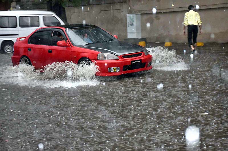 A person pushing his cycle sitting on a kid passing through rain water ...