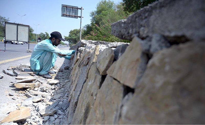 A labourer busy in fixing stones along roadside protection wall at Zero ...