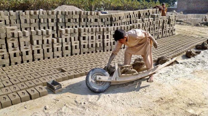 Workers unload clay to make bricks for construction industries at a ...